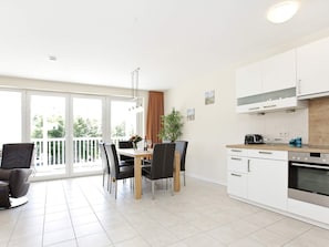 Cozinha moderna com armários brancos, área de jantar com mesa e cadeiras, e varanda com vista.