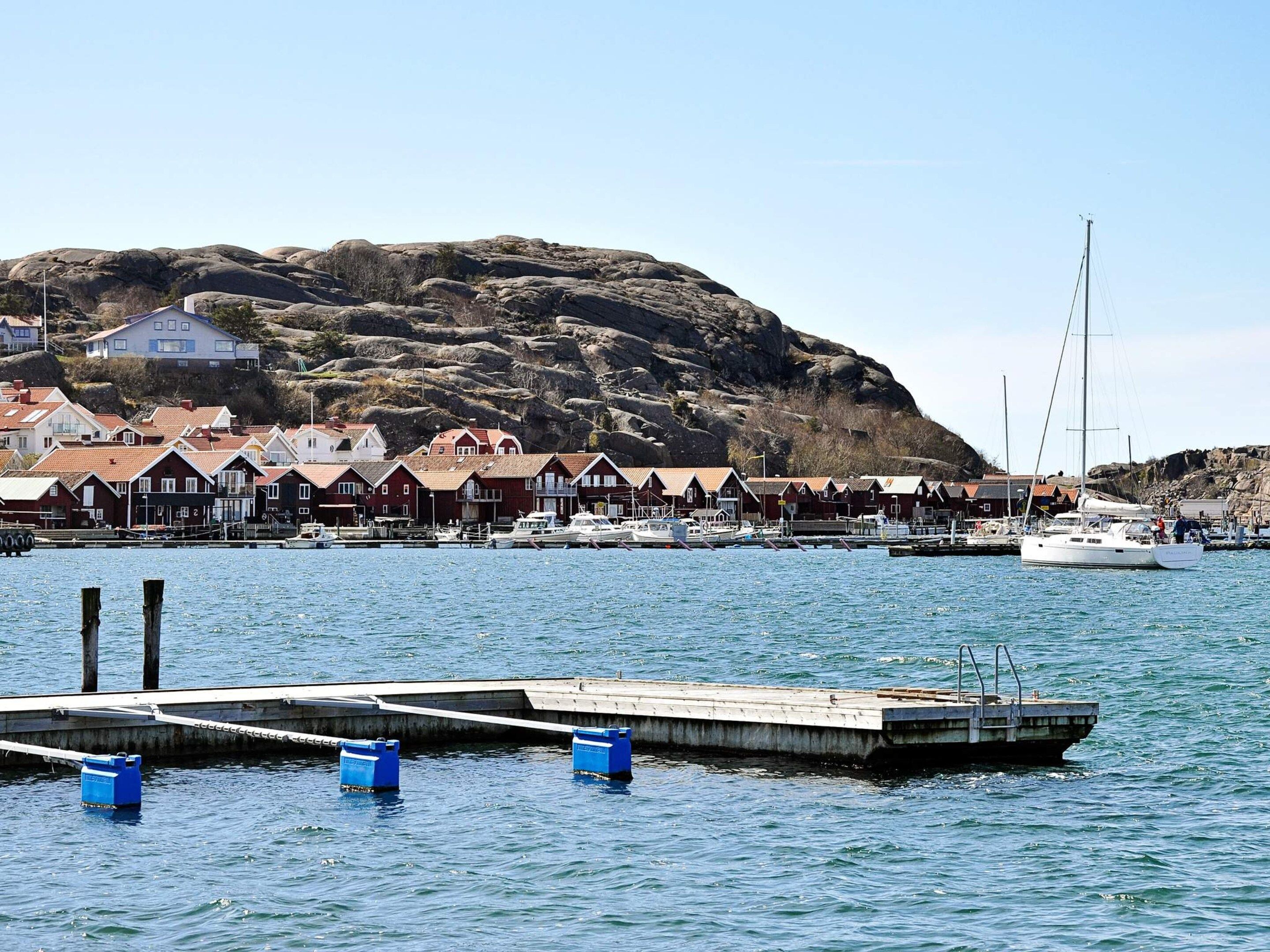 Uma vila costeira com um porto de iates, casas com telhados vermelhos e uma colina rochosa ao fundo.