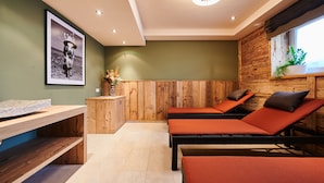 Uma sala de spa com paredes revestidas de madeira, um balcão de recepção e duas macas de massagem com almofadas laranja.