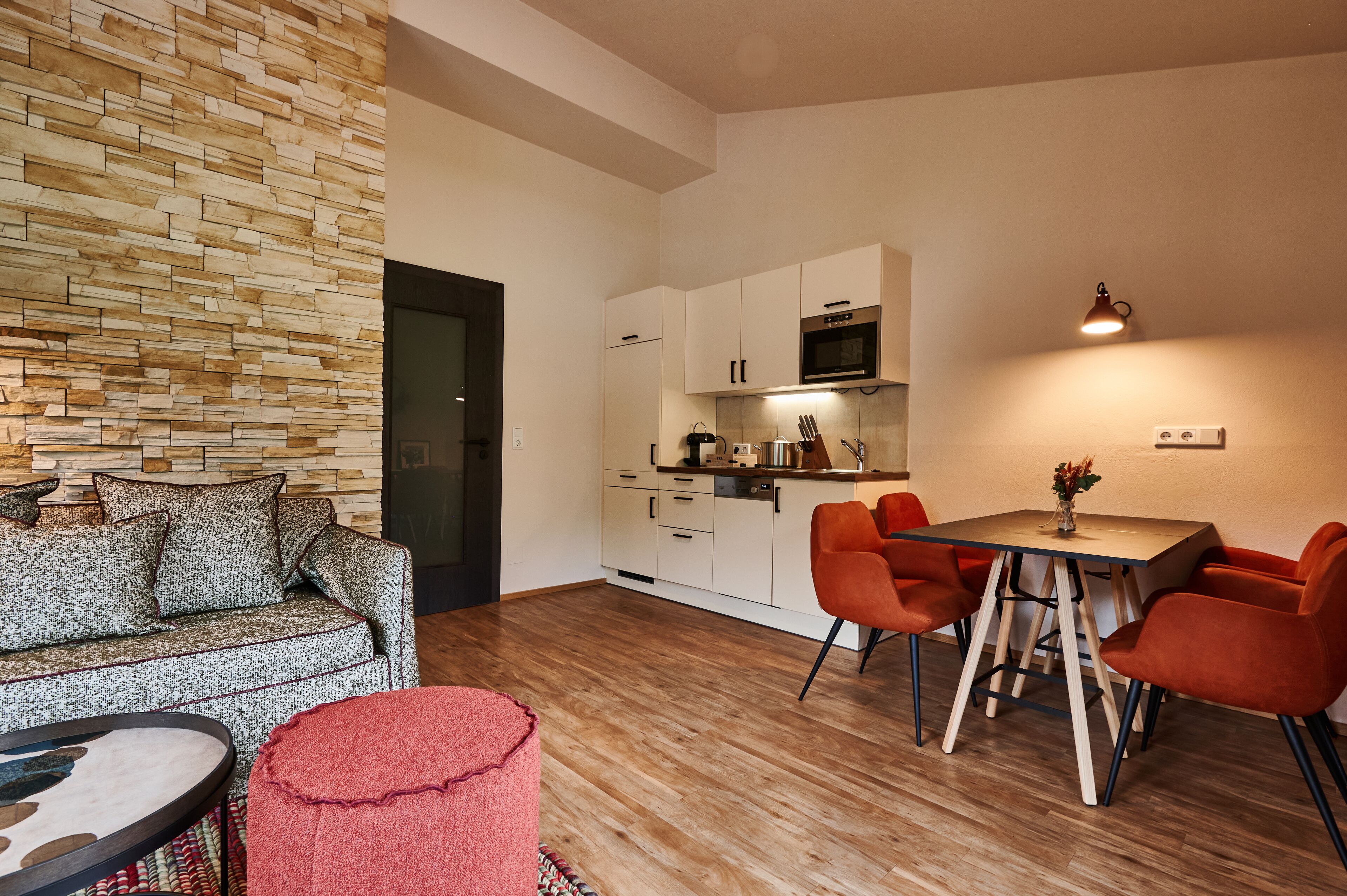 Uma sala de estar moderna com parede de pedra, um sofá, uma mesa de centro e uma área de jantar com mesa e cadeiras.