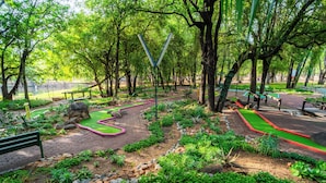 Um parque com um campo de mini golfe, bancos e vegetação exuberante.