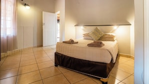 Quarto com cama, porta, janela com cortinas e luminária no teto.