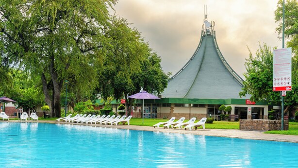 Uma piscina com espreguiçadeiras brancas, um edifício com telhado pontiagudo e uma placa.