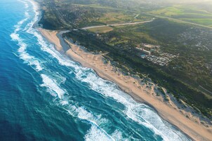 Vista aérea de uma área costeira com praia, estrada e edifícios espalhados.