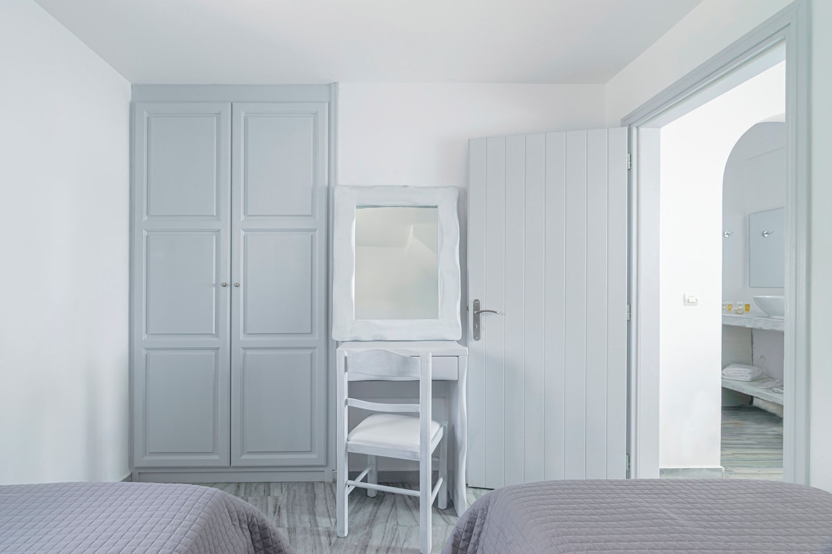 Quarto com duas camas, guarda-roupa, espelho e porta de acesso a um banheiro.