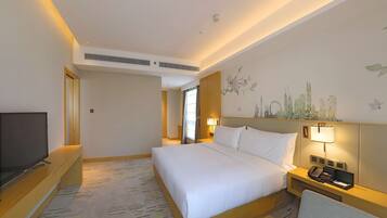 Quarto de hotel com uma cama, mesa de cabeceira com abajur, televisão e um mural com vista para a cidade.