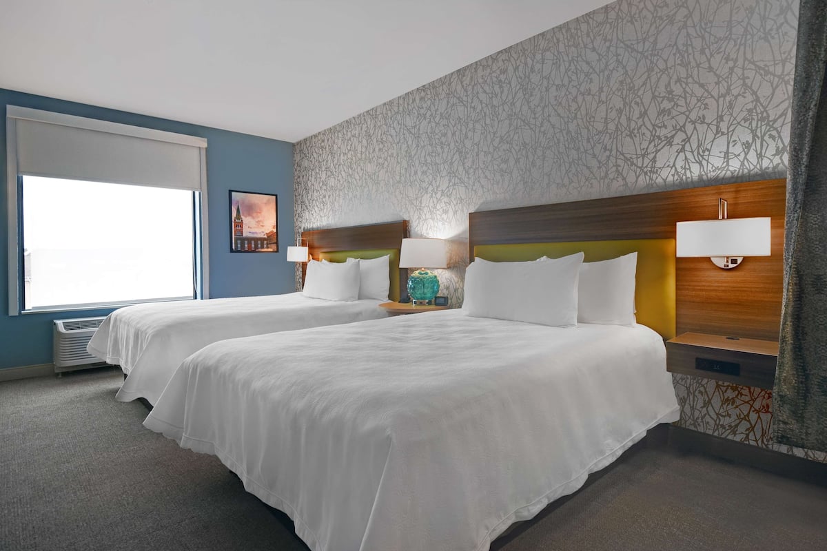 Quarto de hotel com duas camas, uma janela grande e parede com padrão.