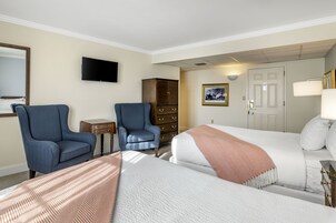 Quarto de hotel com duas camas, televisão, guarda-roupa e escrivaninha com luminária.