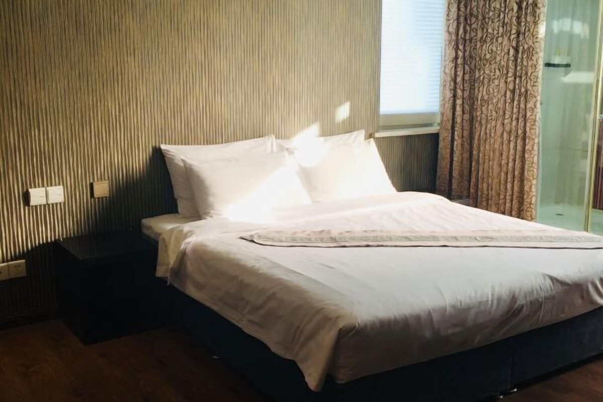 Cama bem arrumada com lençóis brancos em quarto com painéis de madeira nas paredes e porta de vidro.