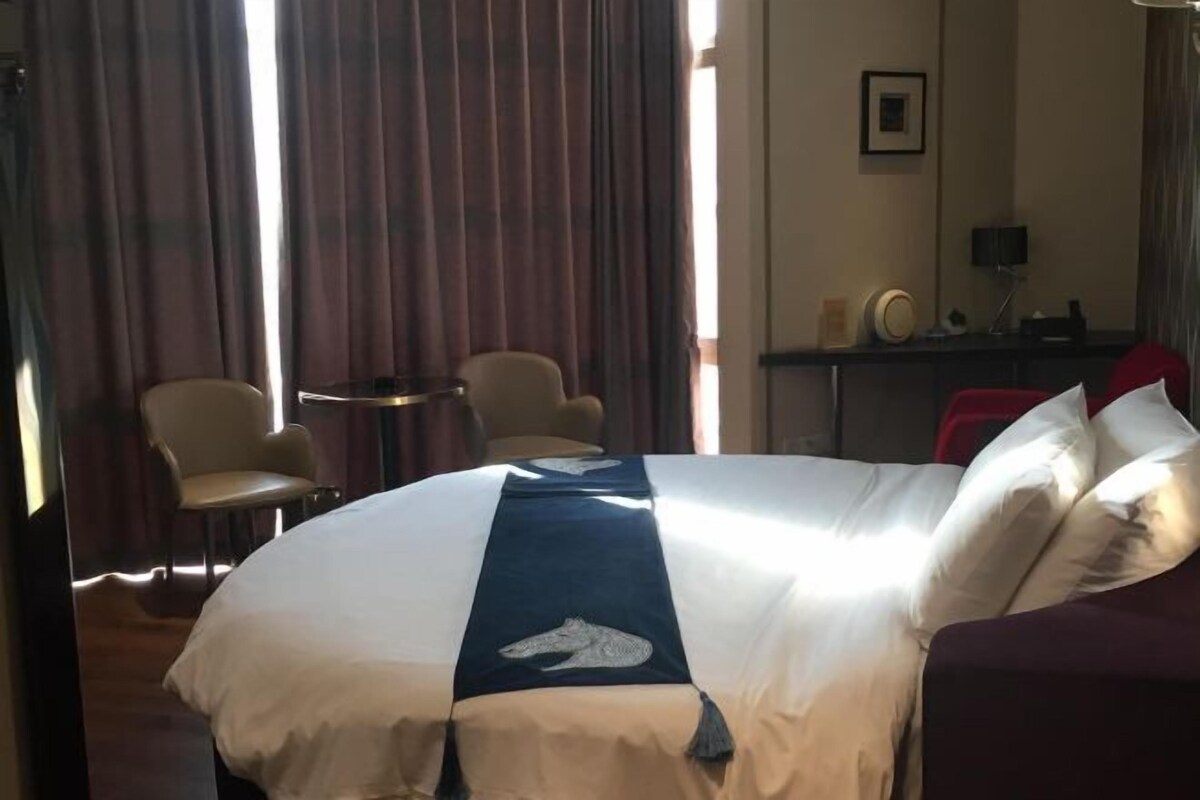 Quarto de hotel com uma cama, duas cadeiras, uma mesinha e uma escrivaninha com abajur.
