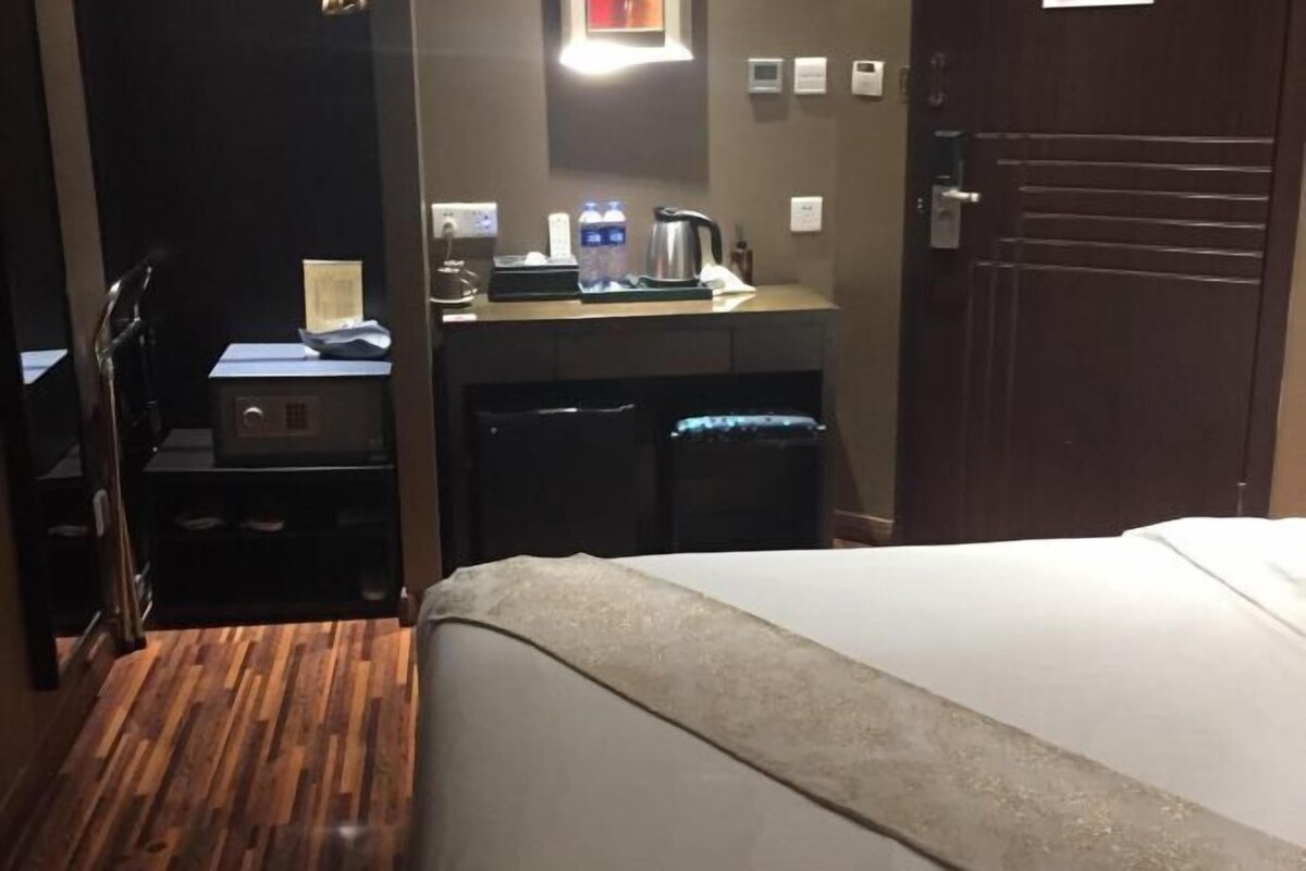 Quarto de hotel com cama, pequeno espaço de cozinha e piso de madeira.