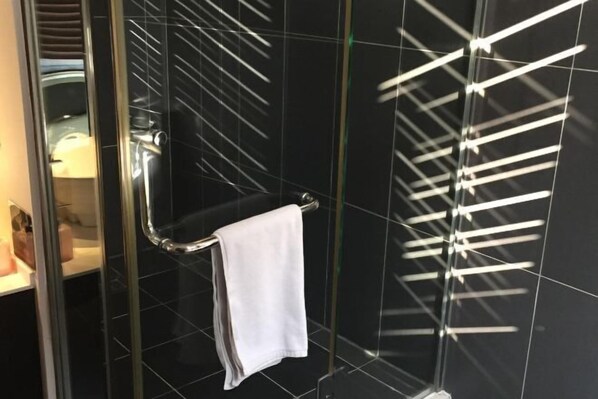 Uma casa de banho moderna com cabine de duche em vidro, uma toalha branca pendurada num suporte de metal e uma pia visível.