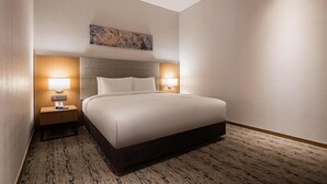 Quarto de hotel com uma cama grande, duas mesas de cabeceira com luminárias, uma cabeceira e piso coberto por carpete.