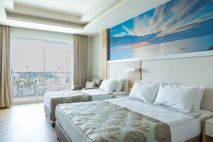 Quarto de hotel com duas camas, uma janela grande com cortinas e uma pintura de um pôr do sol.