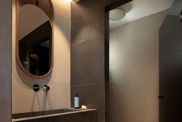 Casa de banho moderna com um espelho grande, chuveiro com cabeça circular e dispensador de sabonete na pia.