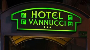 Entrada de hotel com um letreiro de neon, um caminho pavimentado e postes de luz.