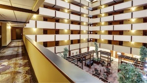 Um saguão de hotel com um átrio central, vários andares e uma área de estar com mesas e cadeiras.