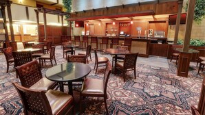 Um saguão de hotel com várias áreas de estar, um bar e uma mesa de recepção.