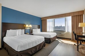 Quarto de hotel com duas camas, uma escrivaninha e uma janela ampla com vista.