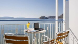 Uma varanda com um laptop, um copo de suco de laranja e duas cadeiras com vista para um mar calmo e ilhas ao longe.