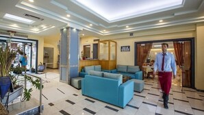 Um saguão de hotel com um amplo sofá azul, uma recepção e uma divisória de vidro.