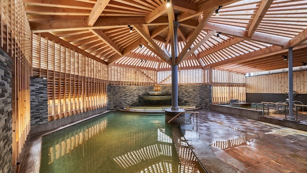 Interior em madeira com piscina central, paredes de pedra e teto inclinado.