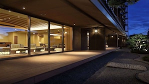 Exterior de hotel moderno com área de estar coberta, portas de vidro que dão para os quartos e um caminho.