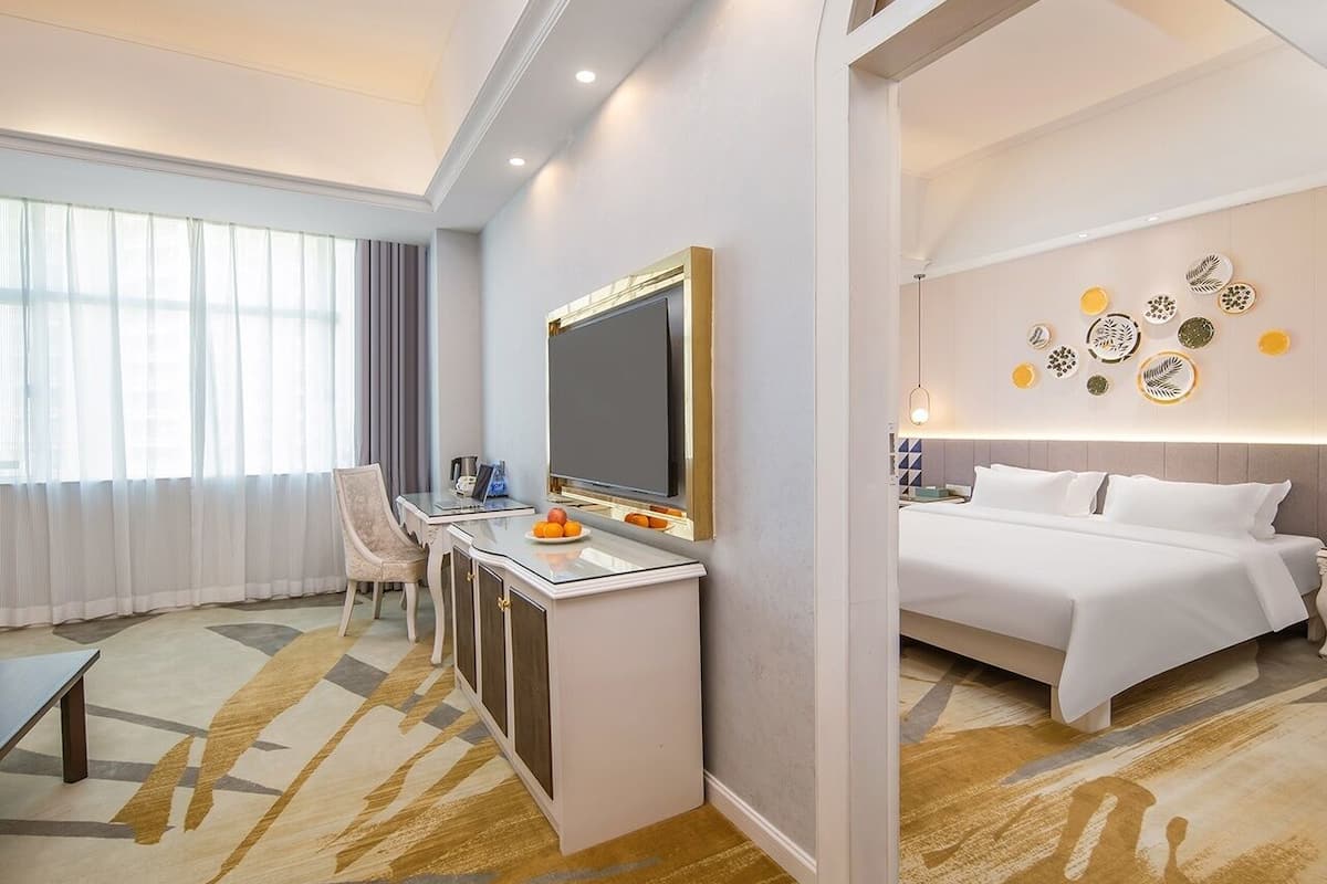 Quarto de hotel com cama, escrivaninha, cadeira, televisão e parede decorada com pratos.