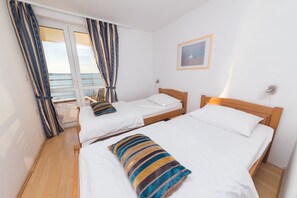 Quarto de hotel com duas camas, cabeceira de madeira, uma janela grande com cortinas e um quadro na parede.