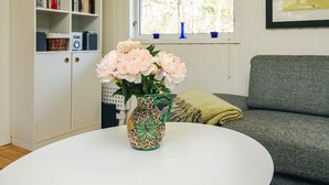 Uma sala de estar com uma mesa de centro branca, uma estante, um sofá cinzento e uma janela com vista para árvores.