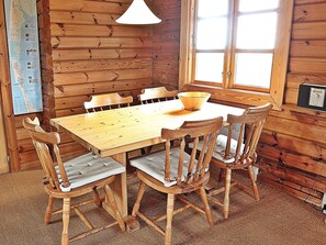 Interior em madeira com uma mesa de jantar, cadeiras, uma janela e um candeeiro fixado na parede.