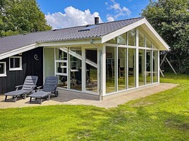 Uma casa moderna com varanda envidraçada, chaminé e um gramado com duas cadeiras de descanso.