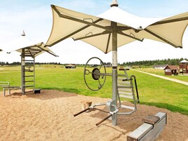 Academia ao ar livre com equipamentos de ginástica, área coberta e piso de areia.