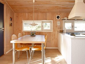 Interior em madeira com mesa de jantar, cadeiras, uma janela e área de cozinha.