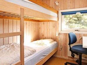 Quarto com beliche, escrivaninha, cadeira, janela e vista para árvores.
