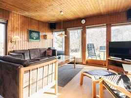 Um quarto com painéis de madeira, um sofá, uma televisão e uma sala de jantar.