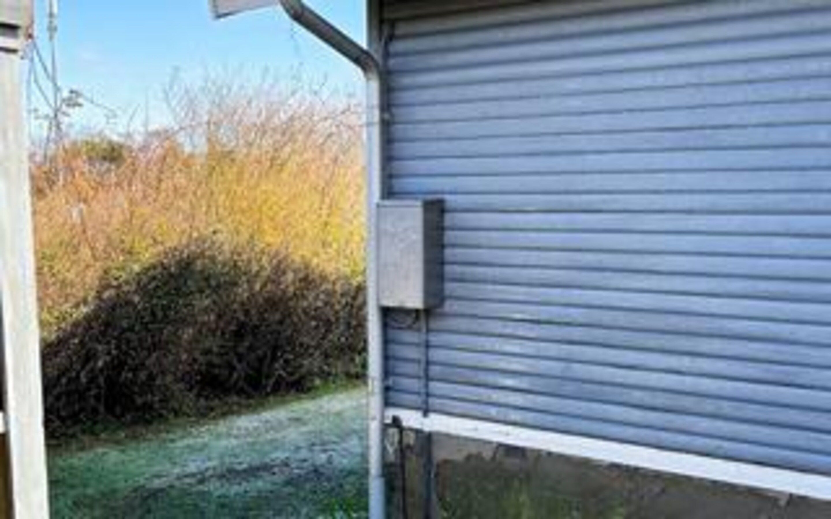 Portão de garagem fechado com uma caixa de serviços na parede.