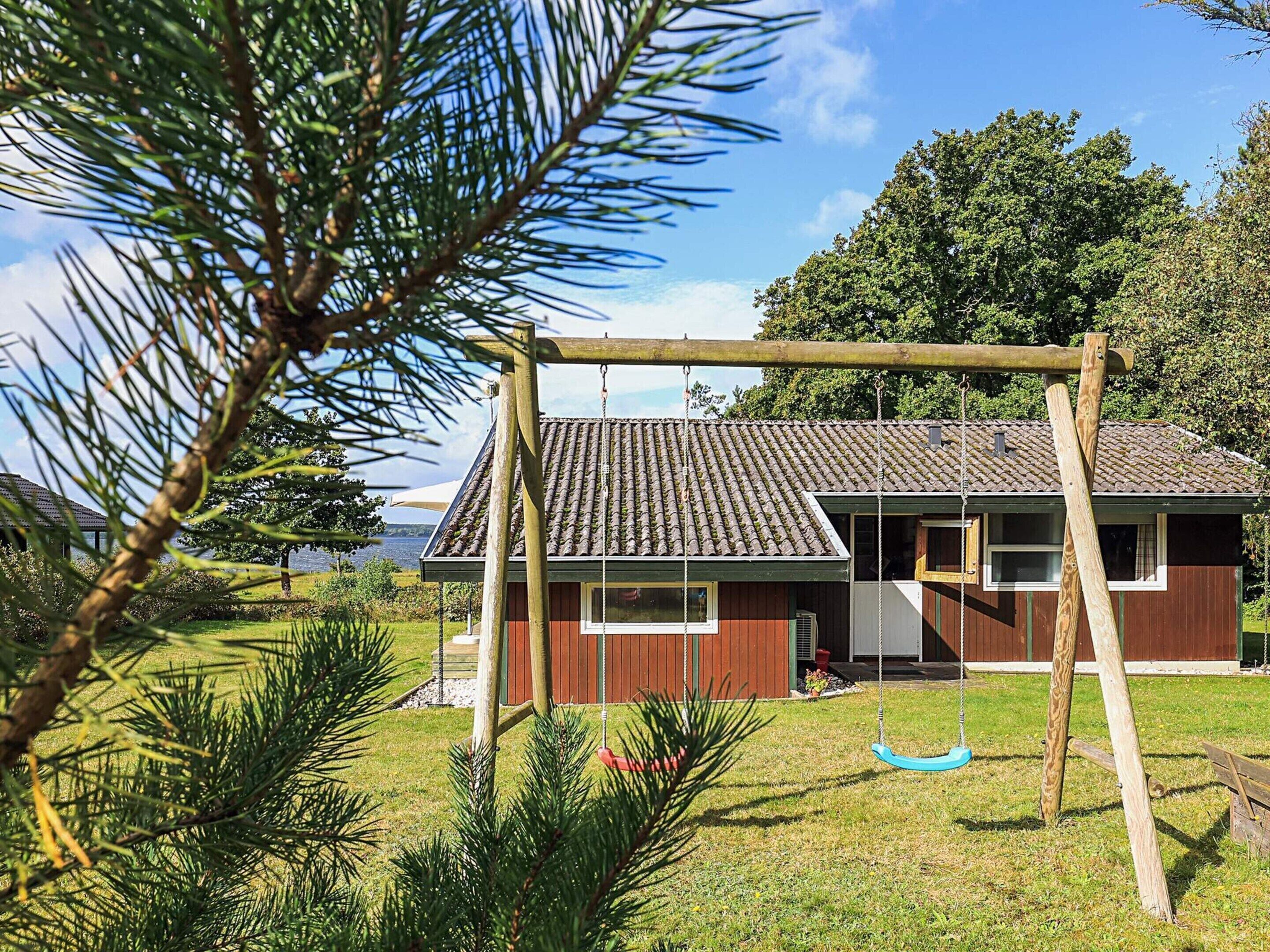 Uma casa com telhado de azulejos, baloiço e vista para um lago.