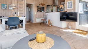 Sala de estar moderna com televisão, sofá e área de refeições.