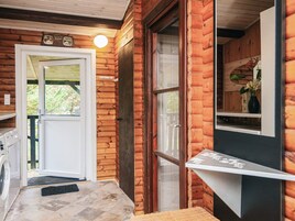 Interior de uma cabana de madeira com porta, um pequeno alpendre, máquina de lavar e espelho.