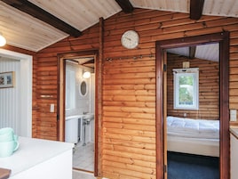 Interior de uma cabana de madeira com banheiro visível, uma cama e um relógio na parede.