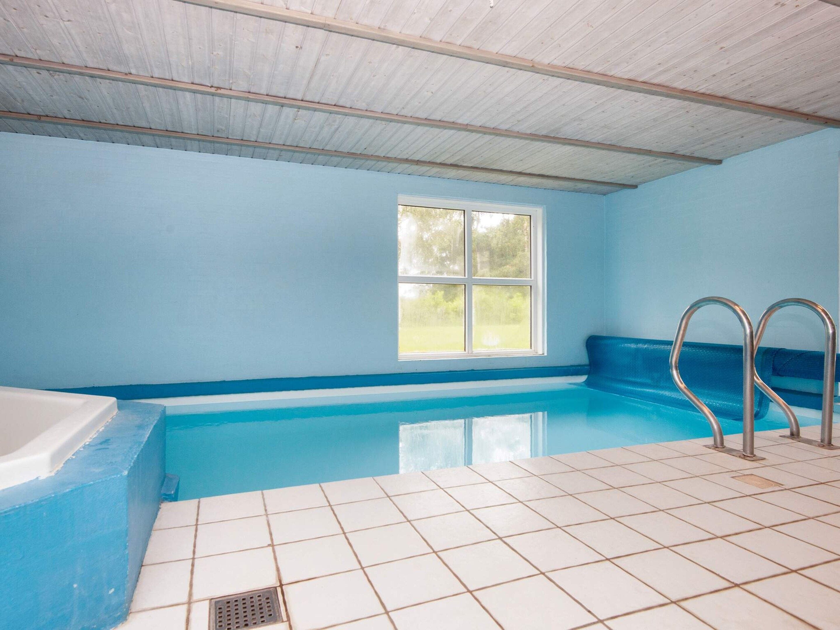 Piscina interna com janela, chão em azulejo e escadas de metal.
