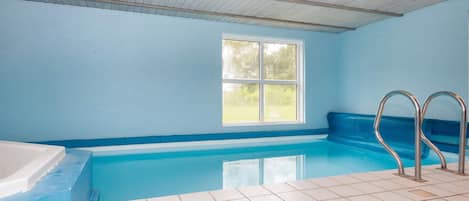Piscina interna com janela, chão em azulejo e escadas de metal.