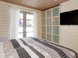 Quarto com cama, televisão, guarda-roupa e janela com cortinas.
