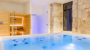 Espaço de spa com hidromassagem, sauna de madeira e paredes de pedra.