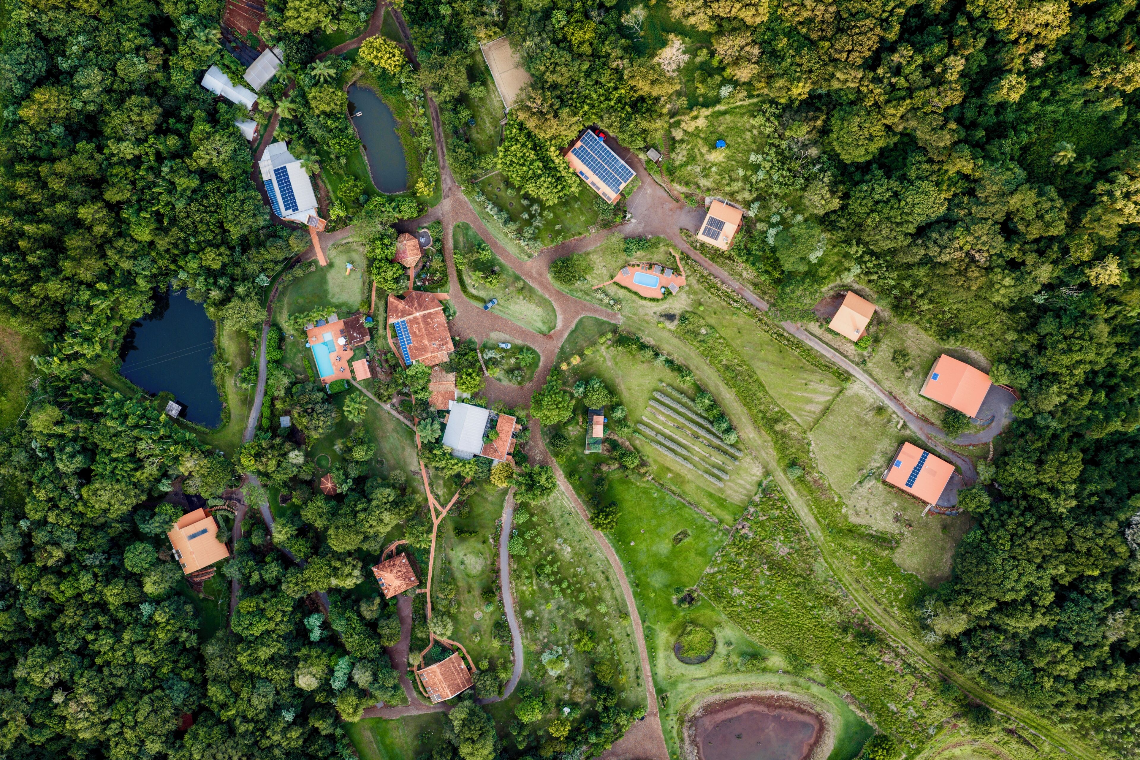 Vista aérea de uma área residencial com várias casas, painéis solares e um pequeno lago.