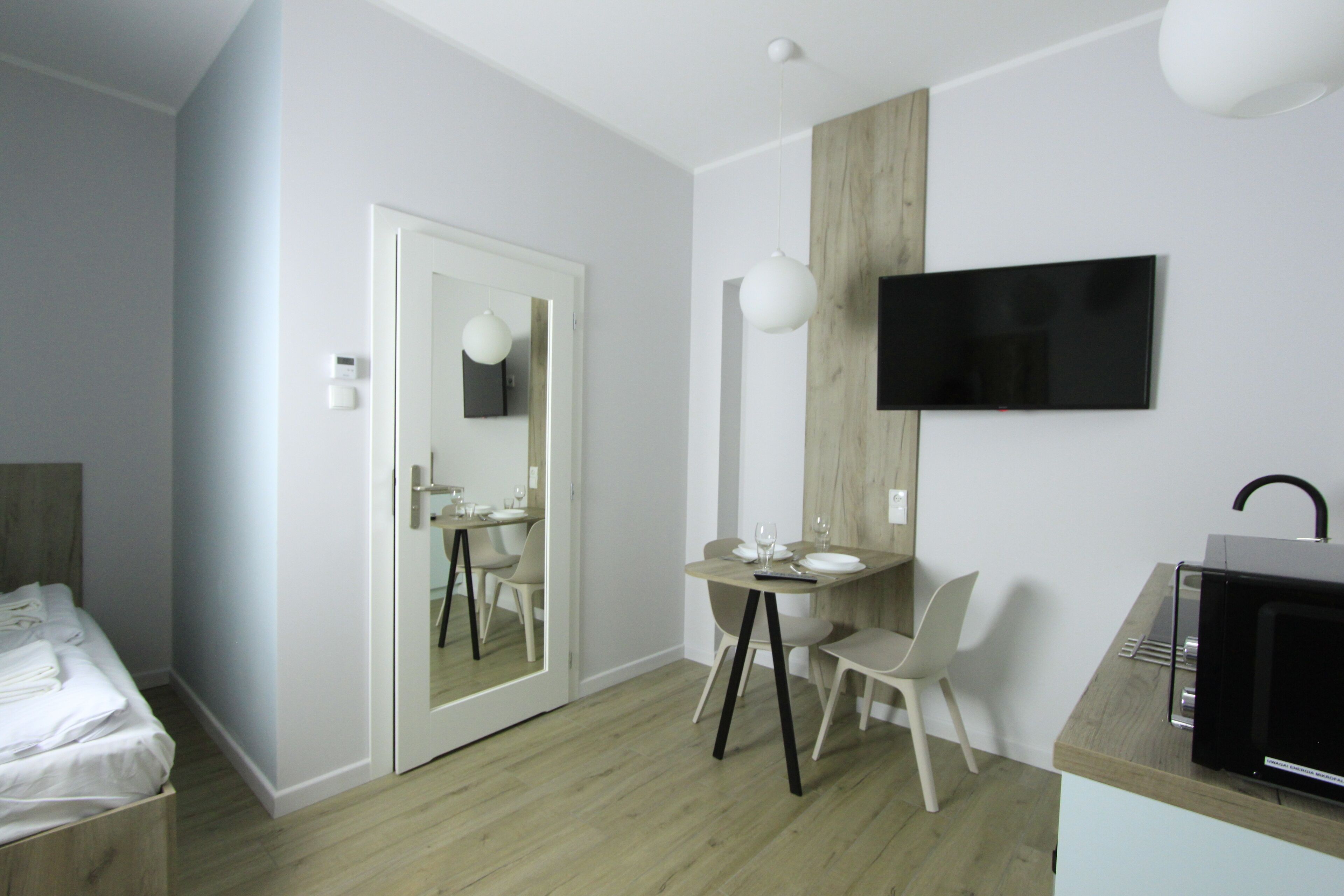 Quarto de hotel moderno com cama, mesa de jantar com cadeiras, TV na parede e micro-ondas na bancada.
