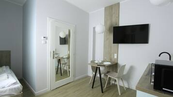Quarto de hotel moderno com cama, mesa de jantar com cadeiras, TV na parede e micro-ondas na bancada.