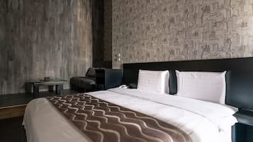 Quarto de hotel moderno com uma cama grande, uma mesinha de apoio e papel de parede estampado.