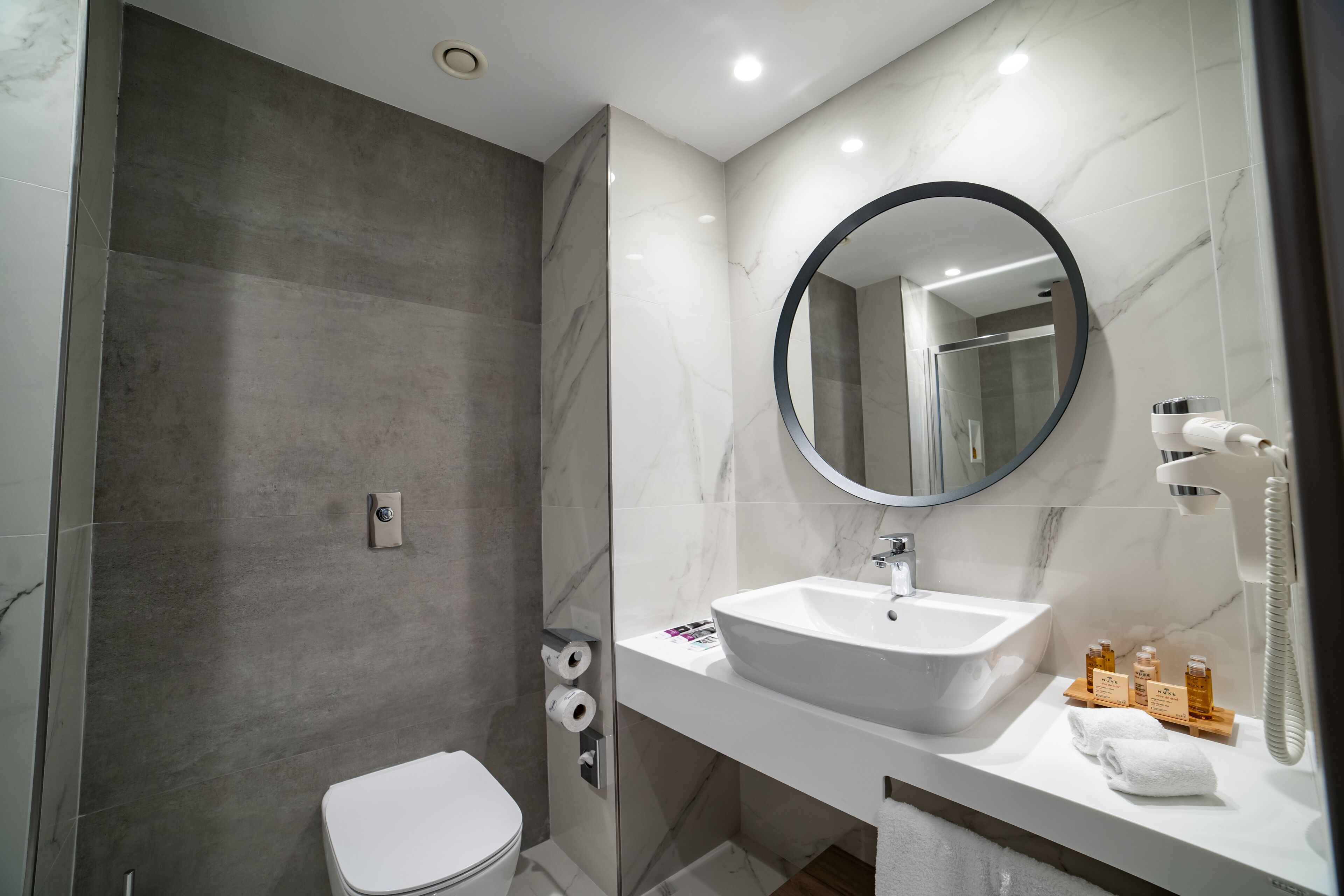Uma casa de banho moderna com uma sanita, um lavatório branco e um espelho grande.